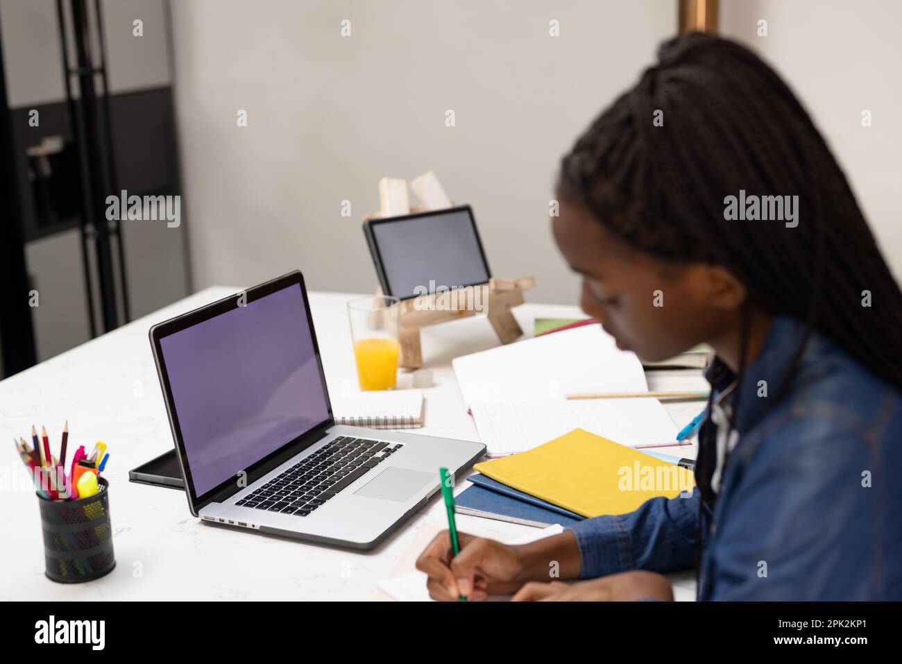 African american teenager girl doing homework, using laptop and tablet ...