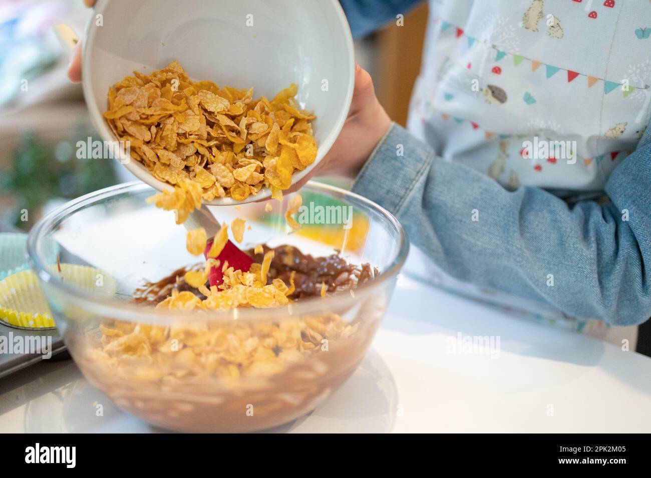 Child mixing and stirring chocolate with cornflakes whilst making ...