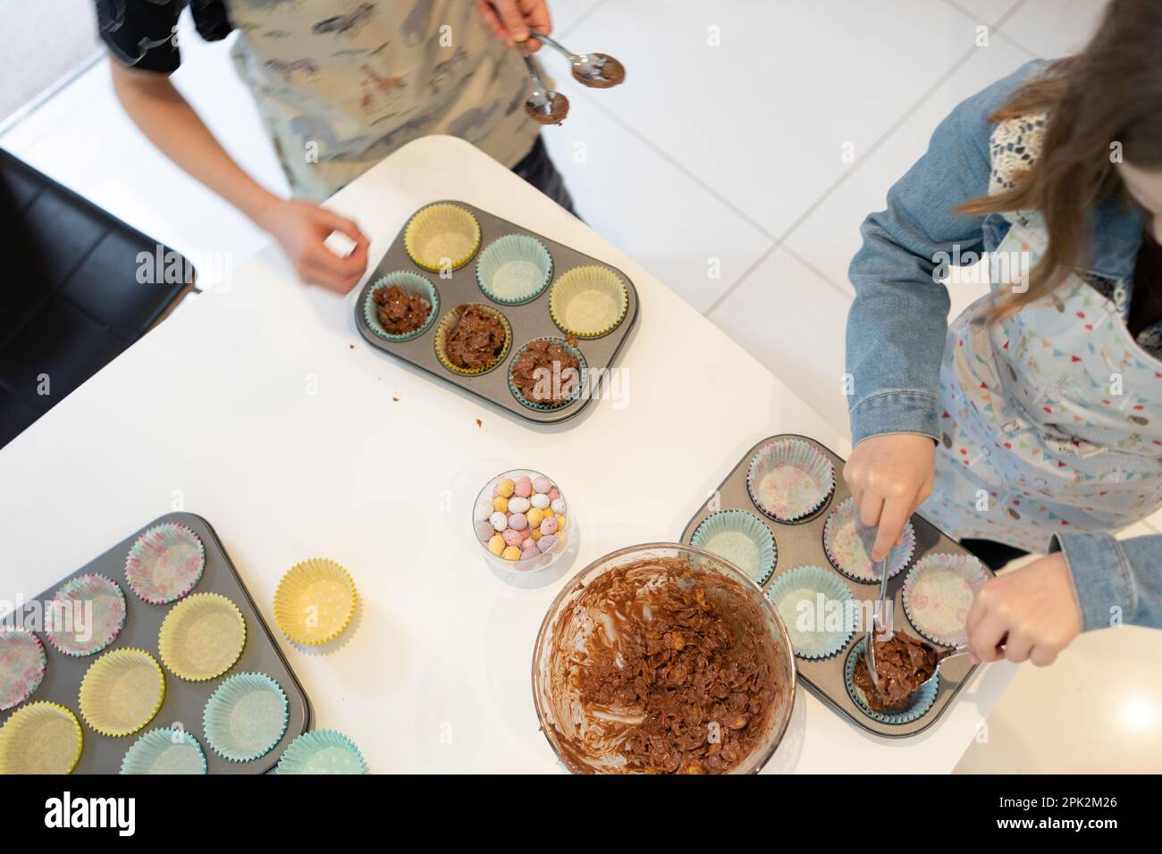 Two children scooping out chocolate cornflake mix whilst making ...
