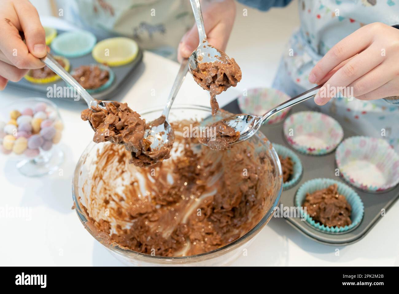 Two children scooping out chocolate cornflake mix whilst making ...