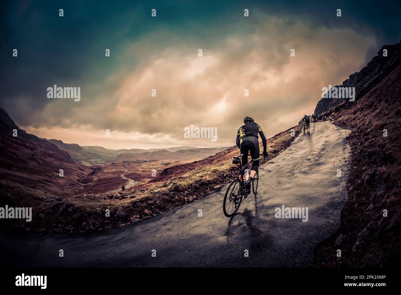 Male road cyclist climbing the steep section of Hardknott Pass, Cumbria ...