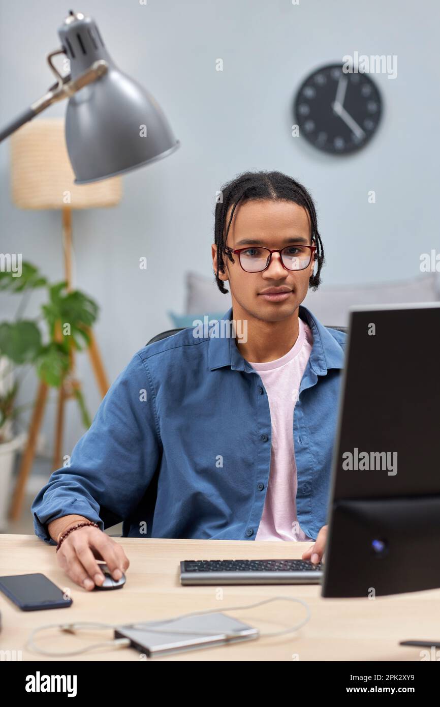 Vertical portrait of young black man using computer at home while ...
