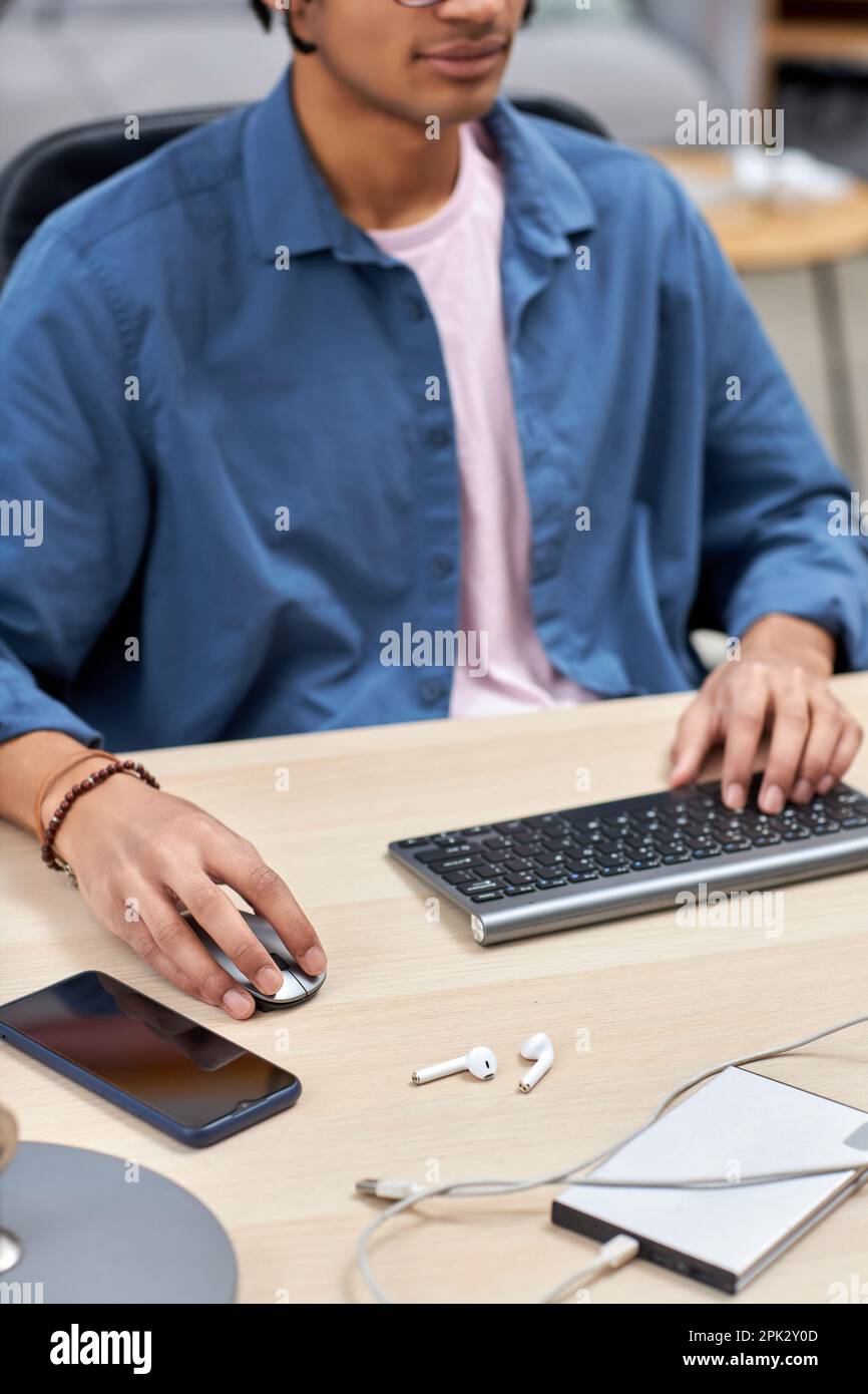 Vertical cropped shot of young black man using computer with focus on male hand holding mouse ...