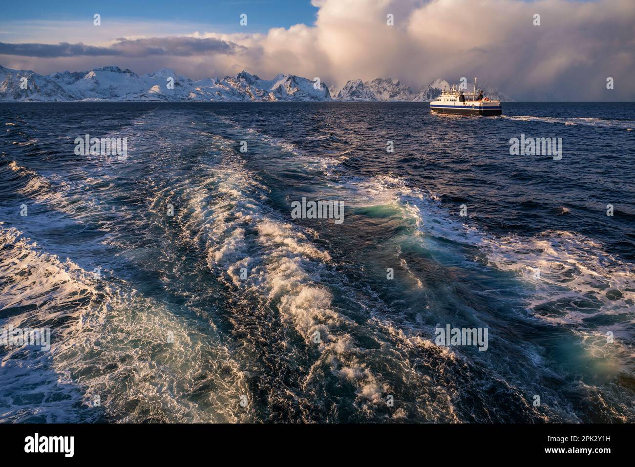 Waves behind boat, ship and snowy mountain on horizon with dramatic sky ...