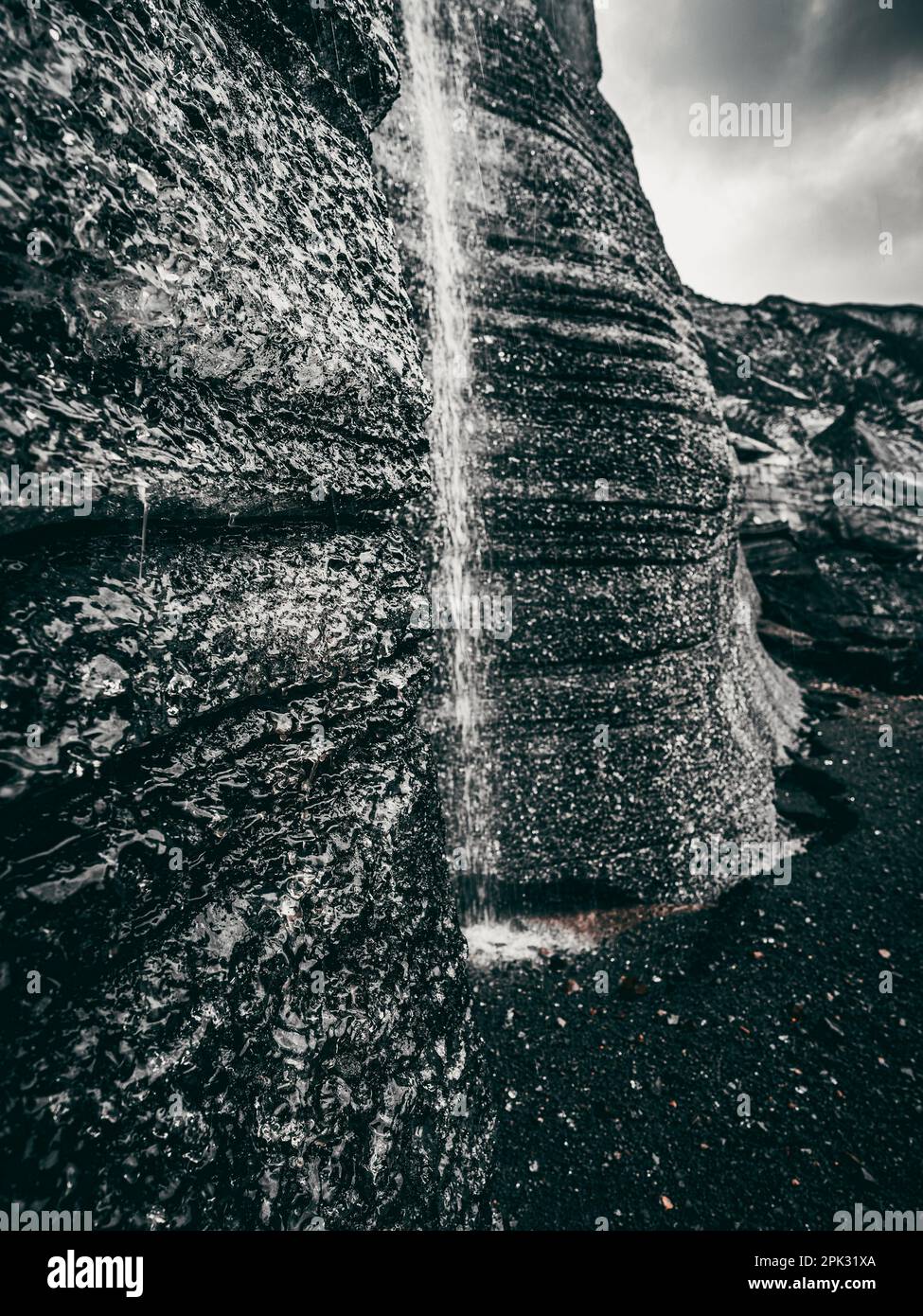 A greyscale of an intricate rock formation with a small stream of water ...