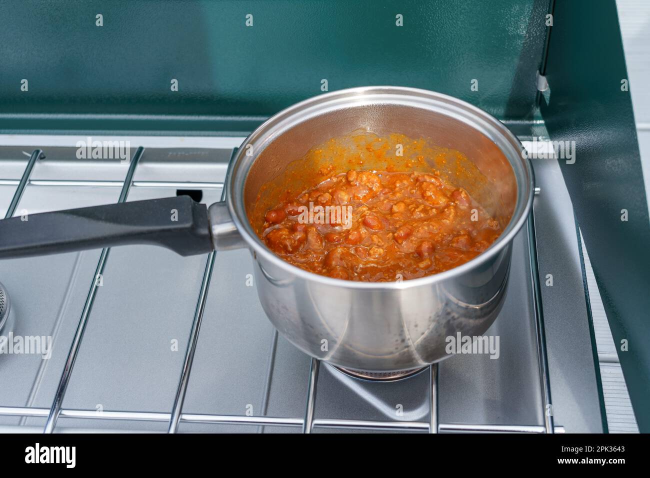 Close-up of cooking chili in a silver pot on an outdoor propane camping ...