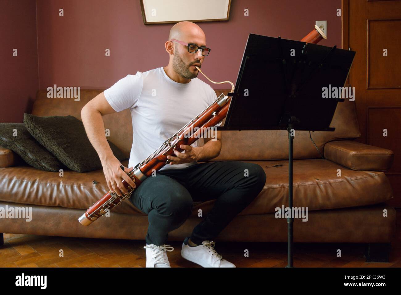 young latino musician man, bald with glasses and white t-shirt, at home ...