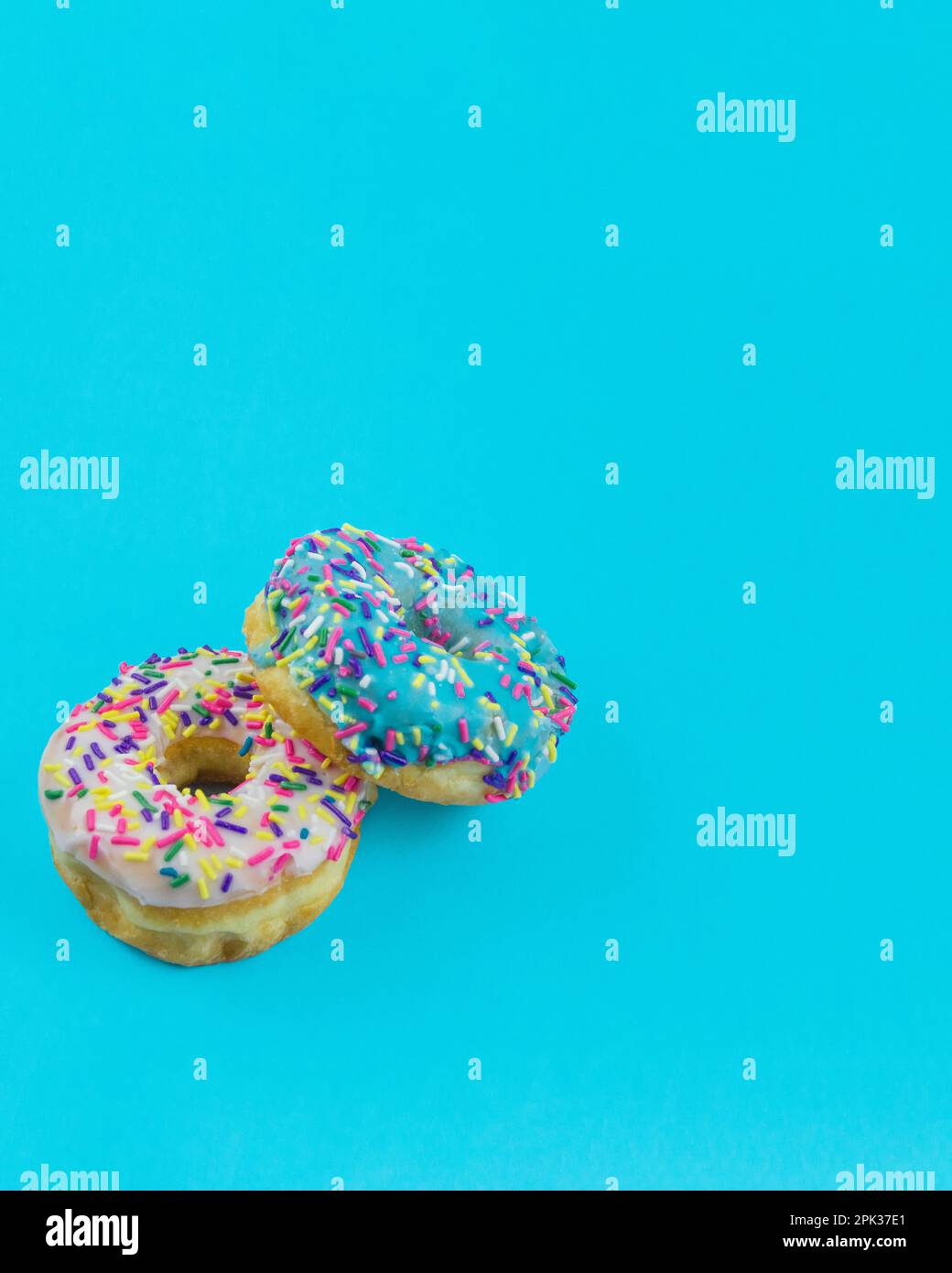 Two donuts with icing and sprinkles on a plain blue background with ...