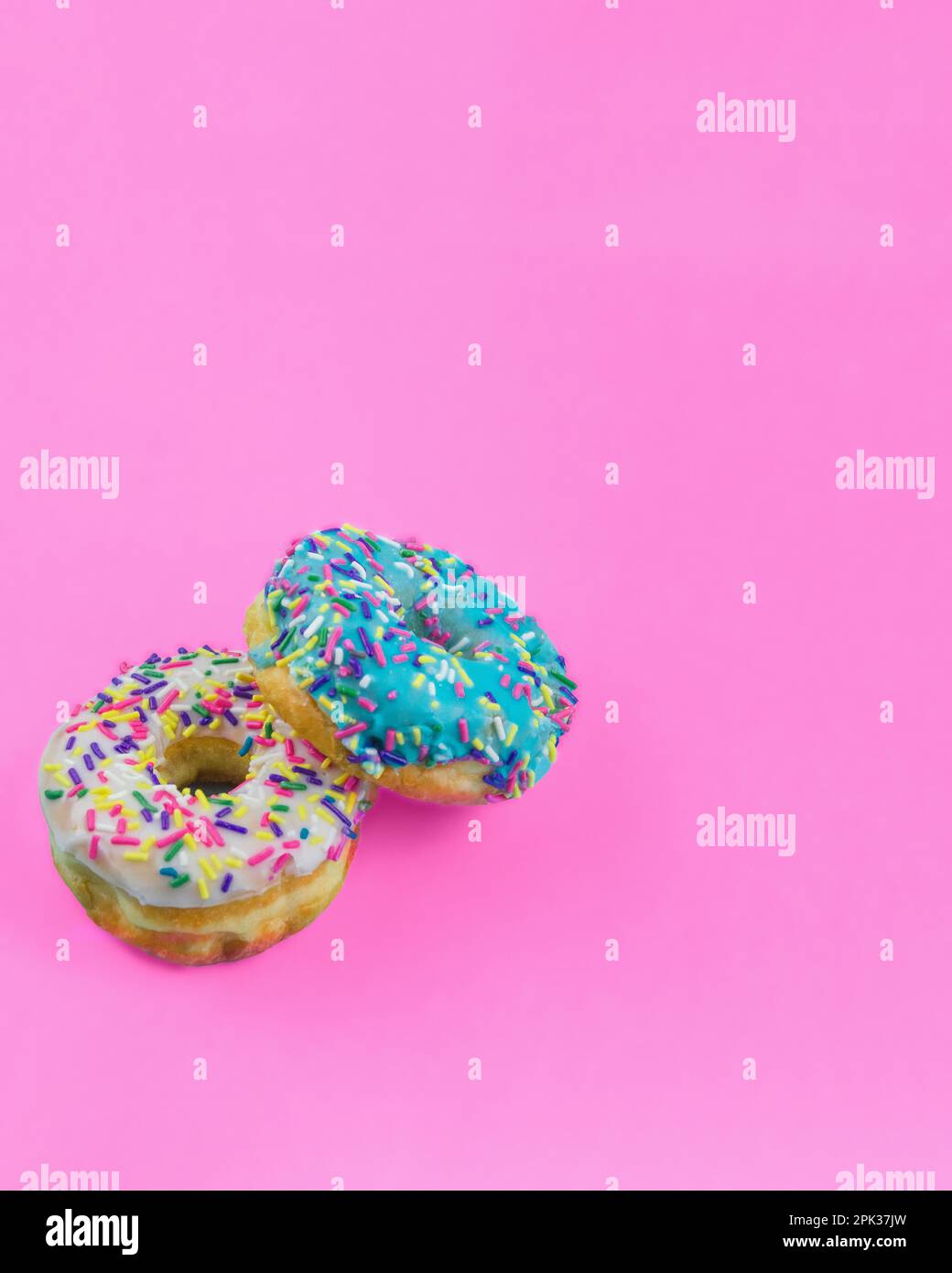 Two donuts with icing and sprinkles on a plain pink background with ...