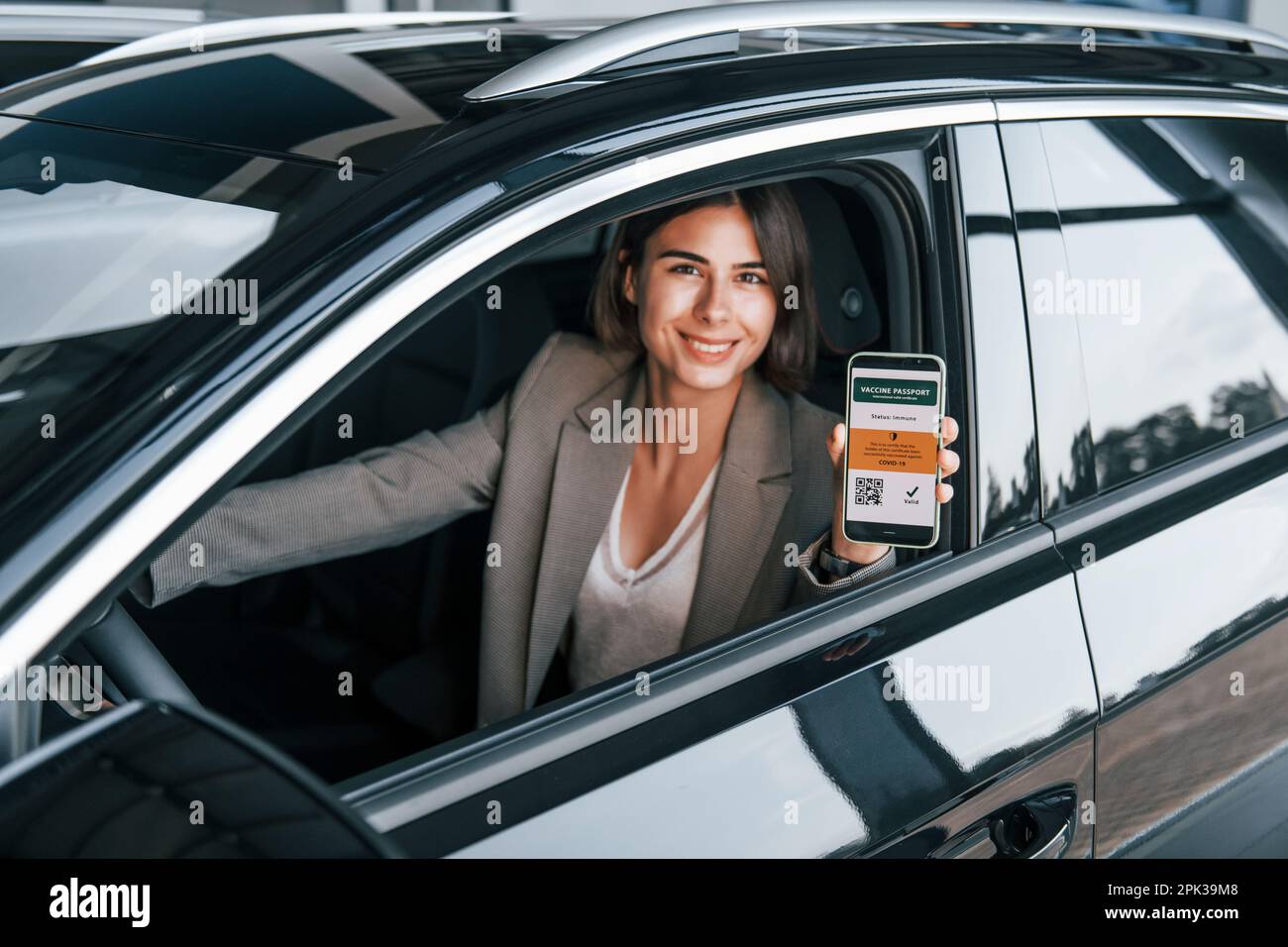 Holding smartphone with digital vaccine passport. Woman testing new car ...