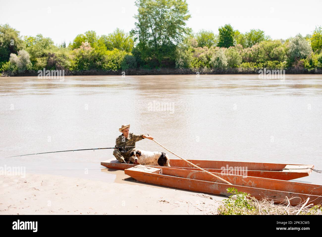 Pensive male fisher with long stick pushing off from bank, going ...