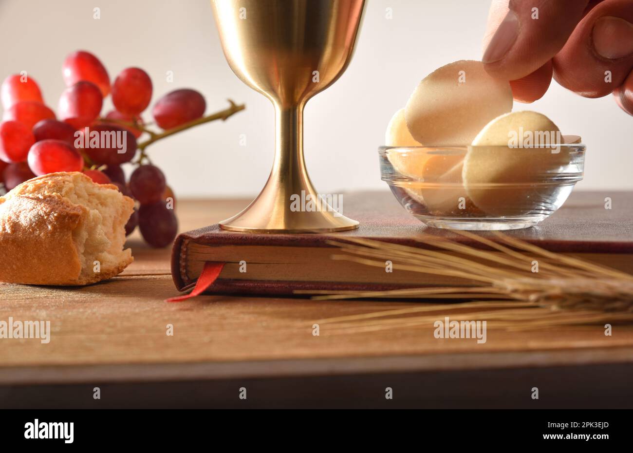 Detail of hand picking up consecrated host in container on wooden table ...