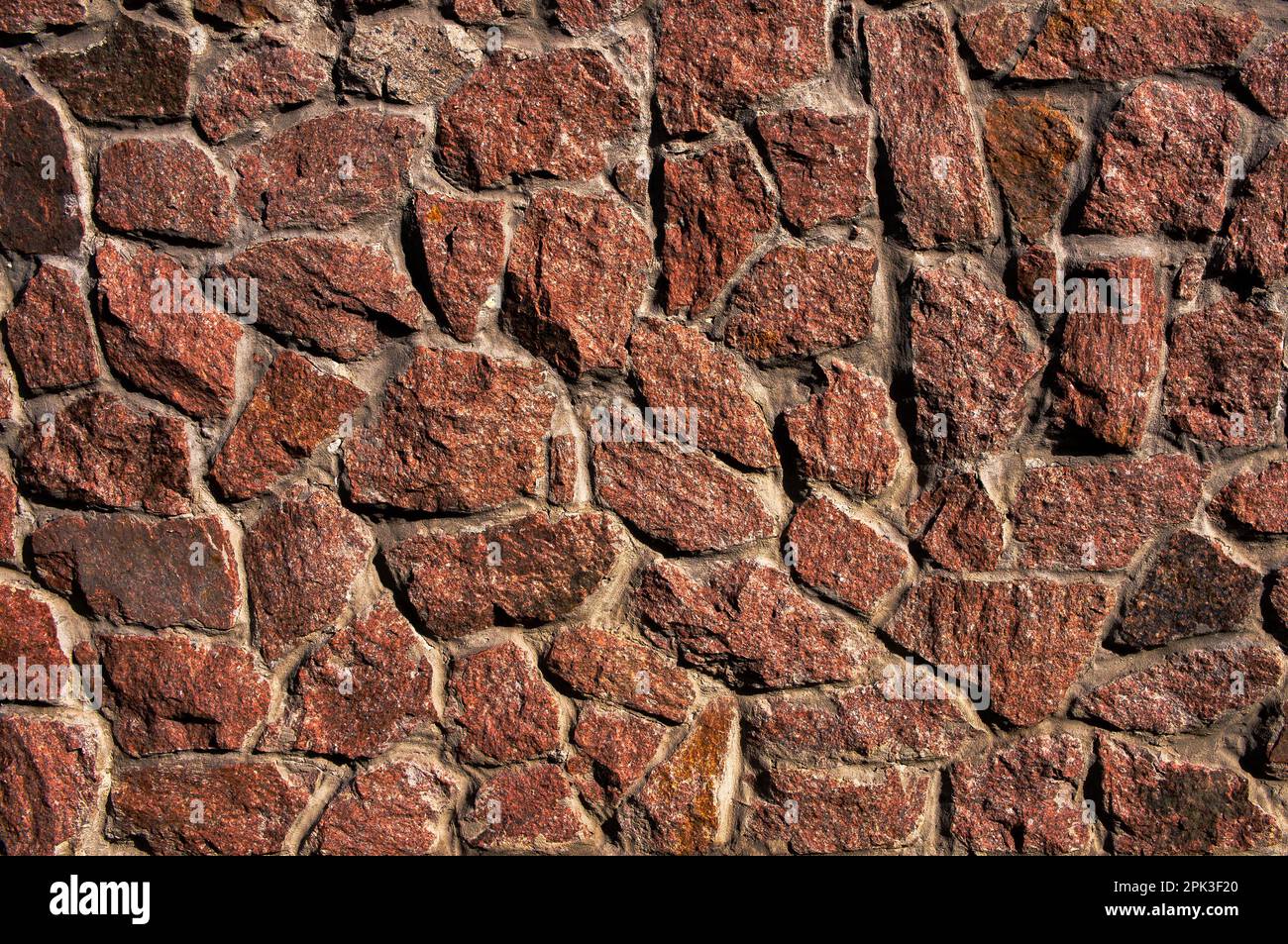 A wall made of rough, red, hewn natural stones. Can be used as a ...