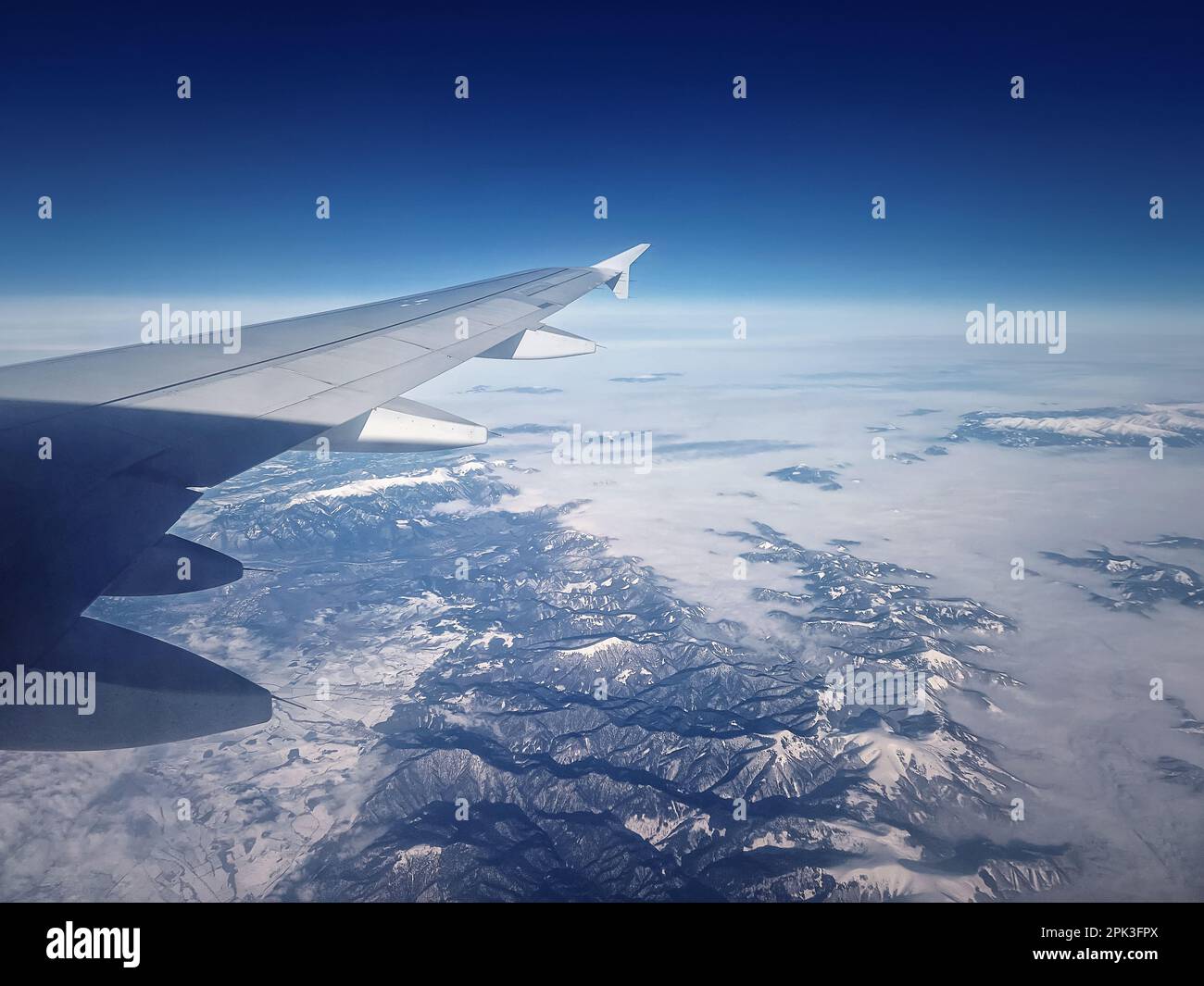 Plane flight above the Carpathian Mountains snowy peaks. Blue skyline ...
