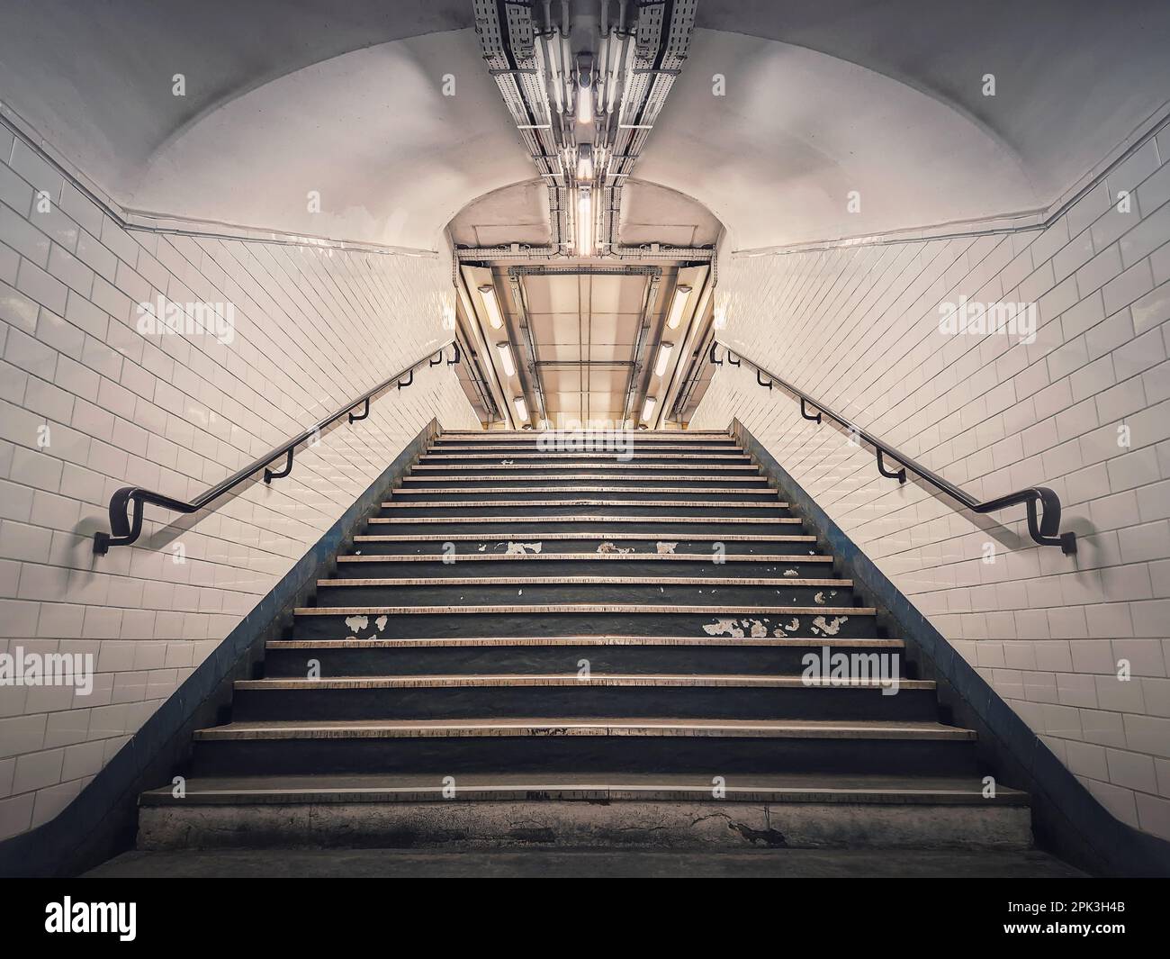 Subway corridor with white tile on walls and glowing lights above a the stairs passage ...