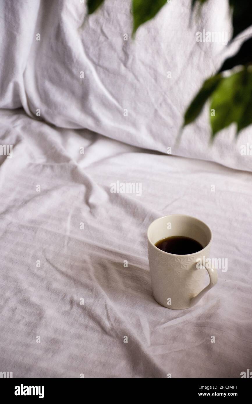 A steaming hot morning coffee resting on a bed, with a green leaf ...