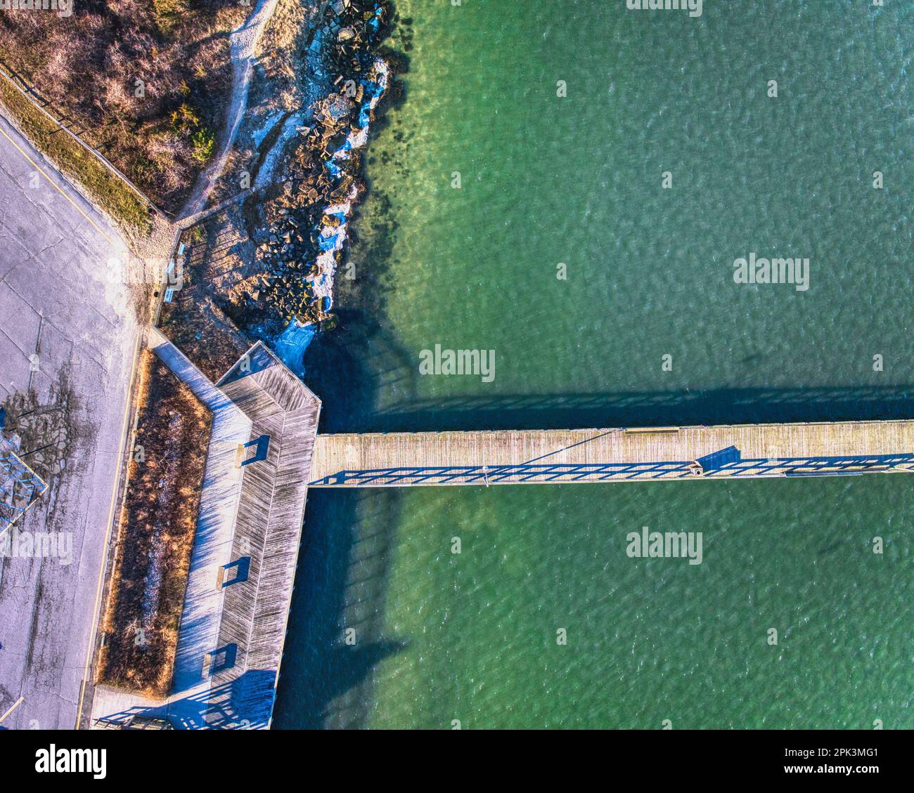 An aerial top view of a wooden pier arching over a tranquil body of ...