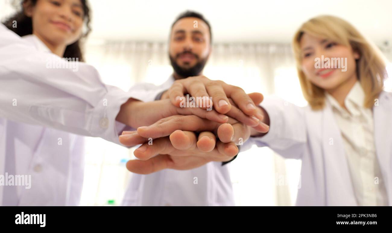 Group of diverse researcher team with white gowns holding hands ...