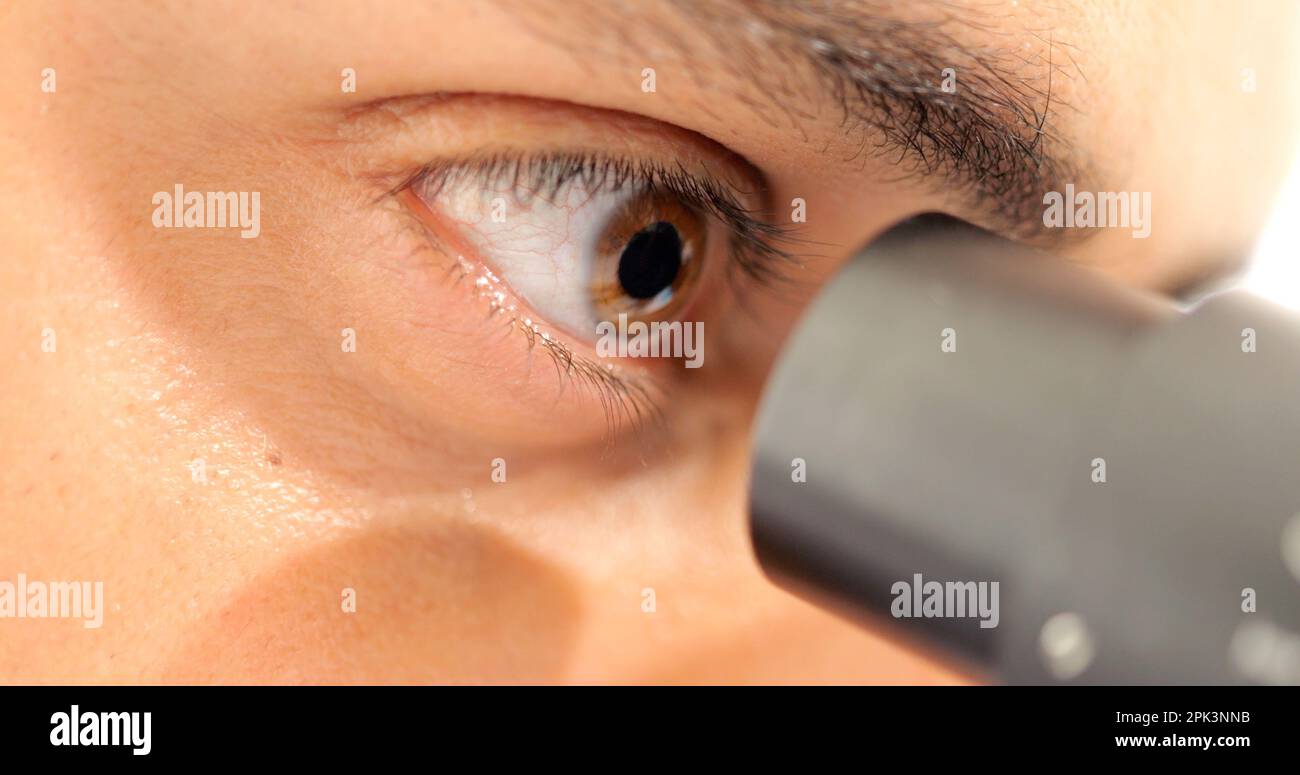 Eye of professional male scientist looking through microscope in ...