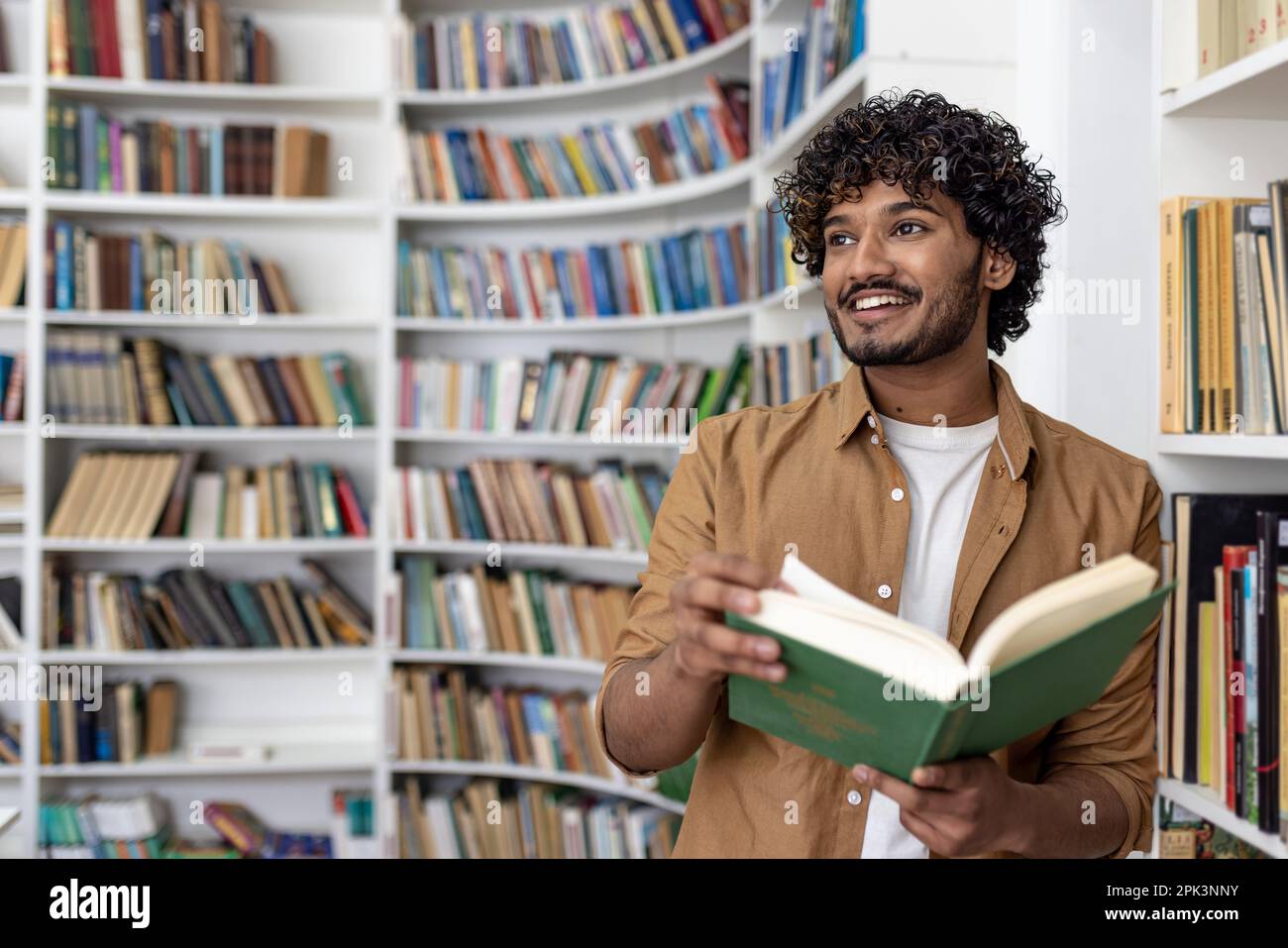 Young hispanic student reading a book while standing inside an academic ...
