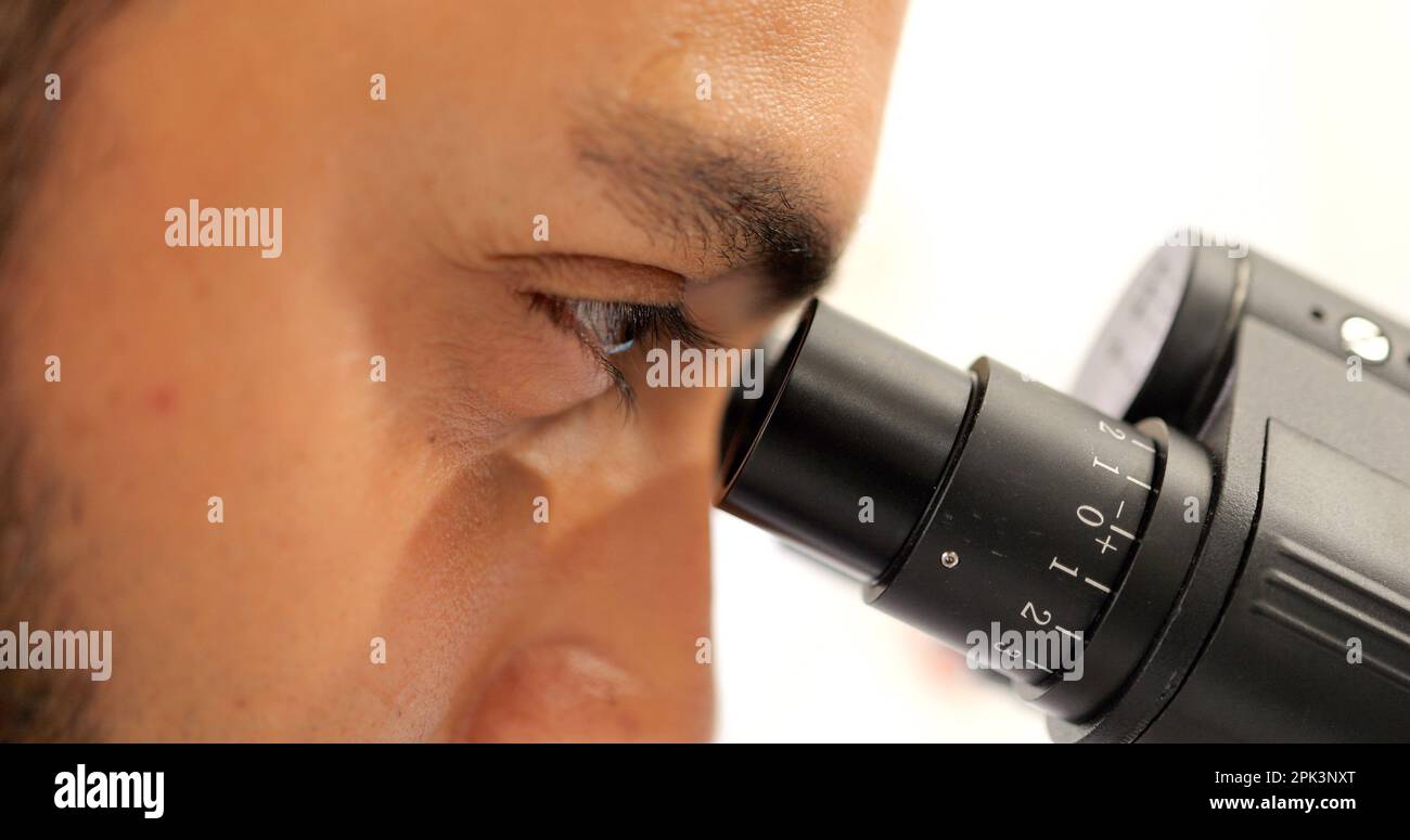 Eye of professional male scientist looking through microscope in ...