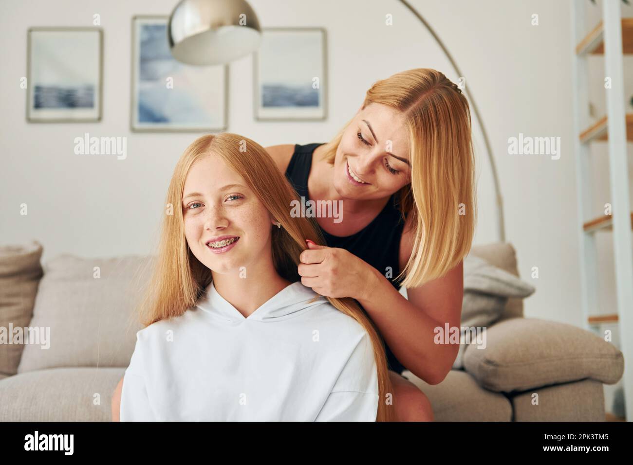 Parent helping with hair. Female teenager with her mother is at home at ...