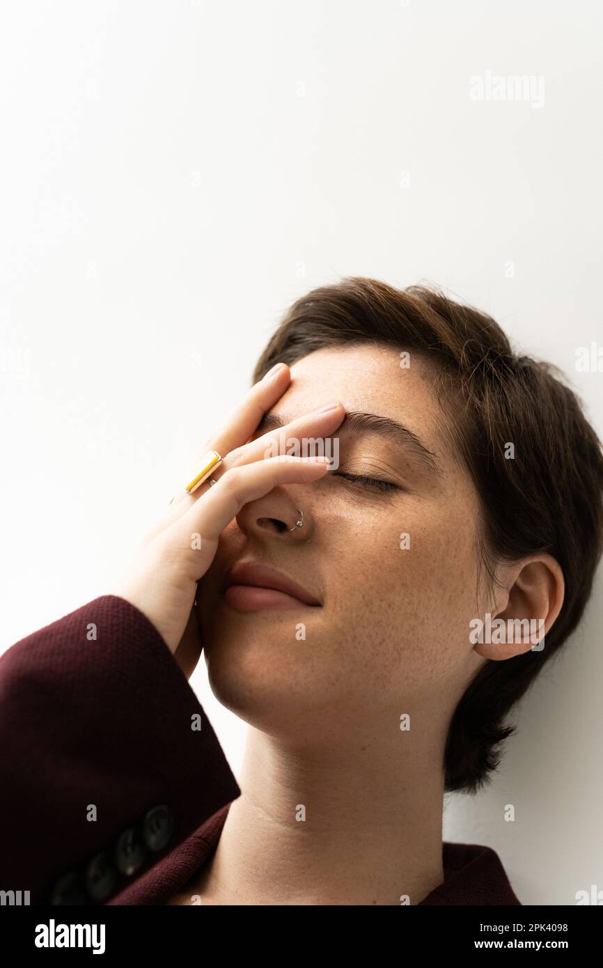 young brunette woman with freckles obscuring face with hand on grey ...