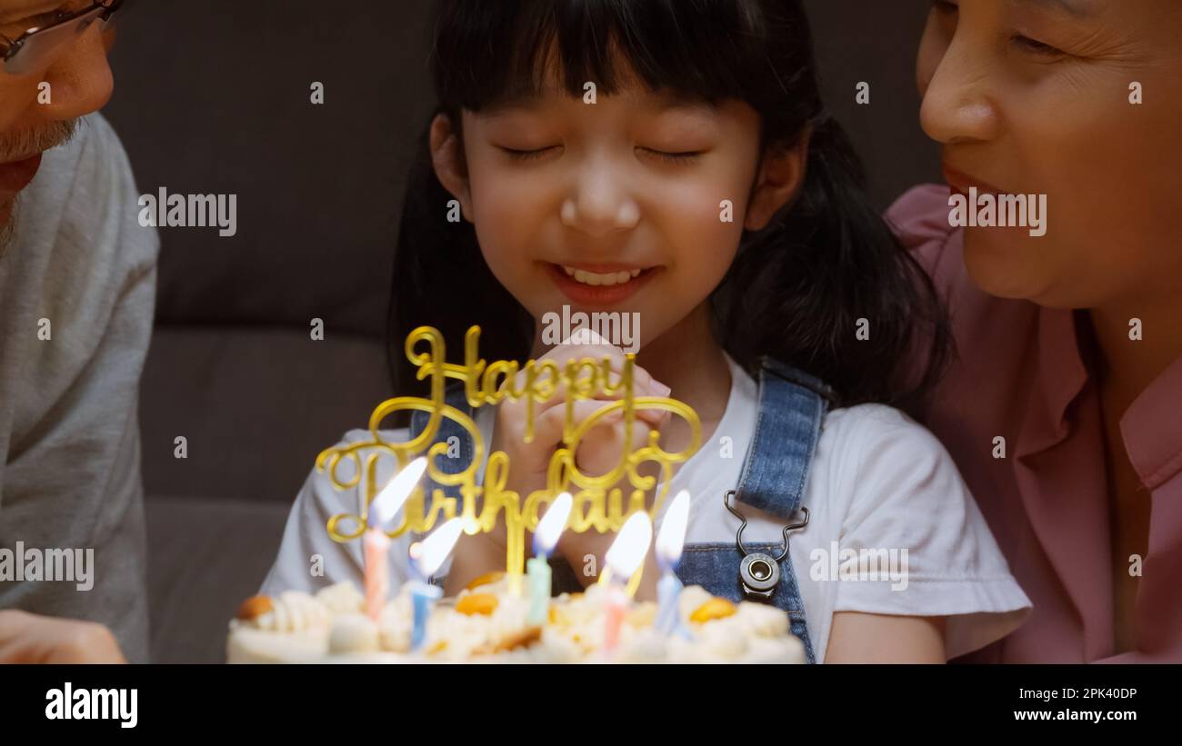 Happy girl surrounded by family making wish and blowing out candles on ...