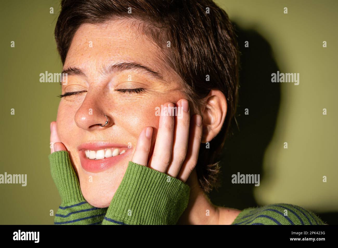 portrait of overjoyed woman with freckles and nose piercing touching ...