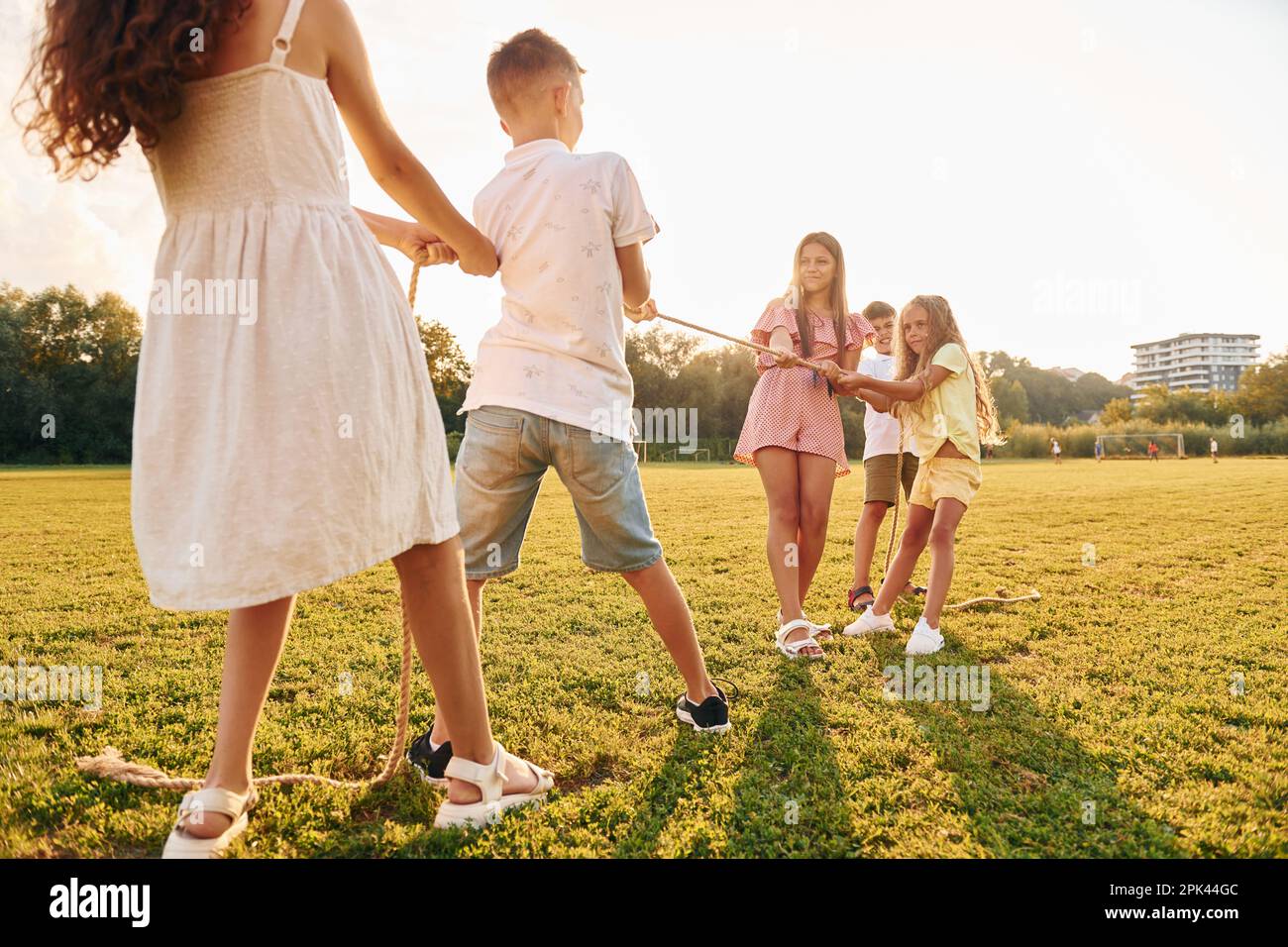 Playing tug of war. Group of happy kids is outdoors on the sportive ...