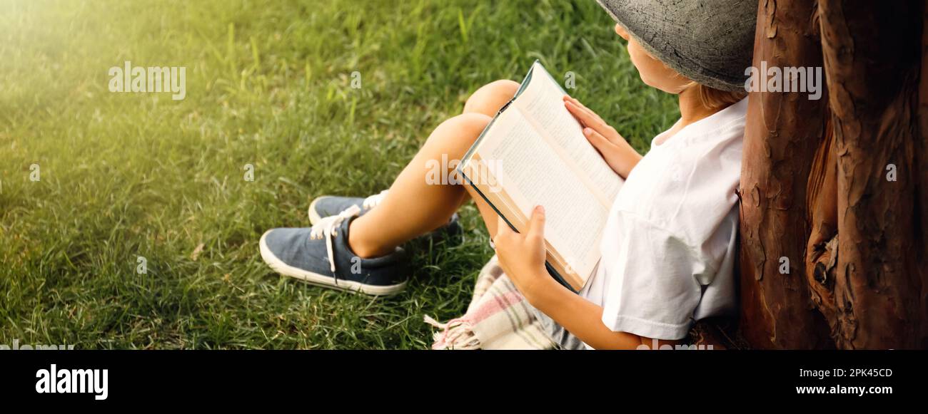 Cute little boy reading book on green grass near tree in park, space ...