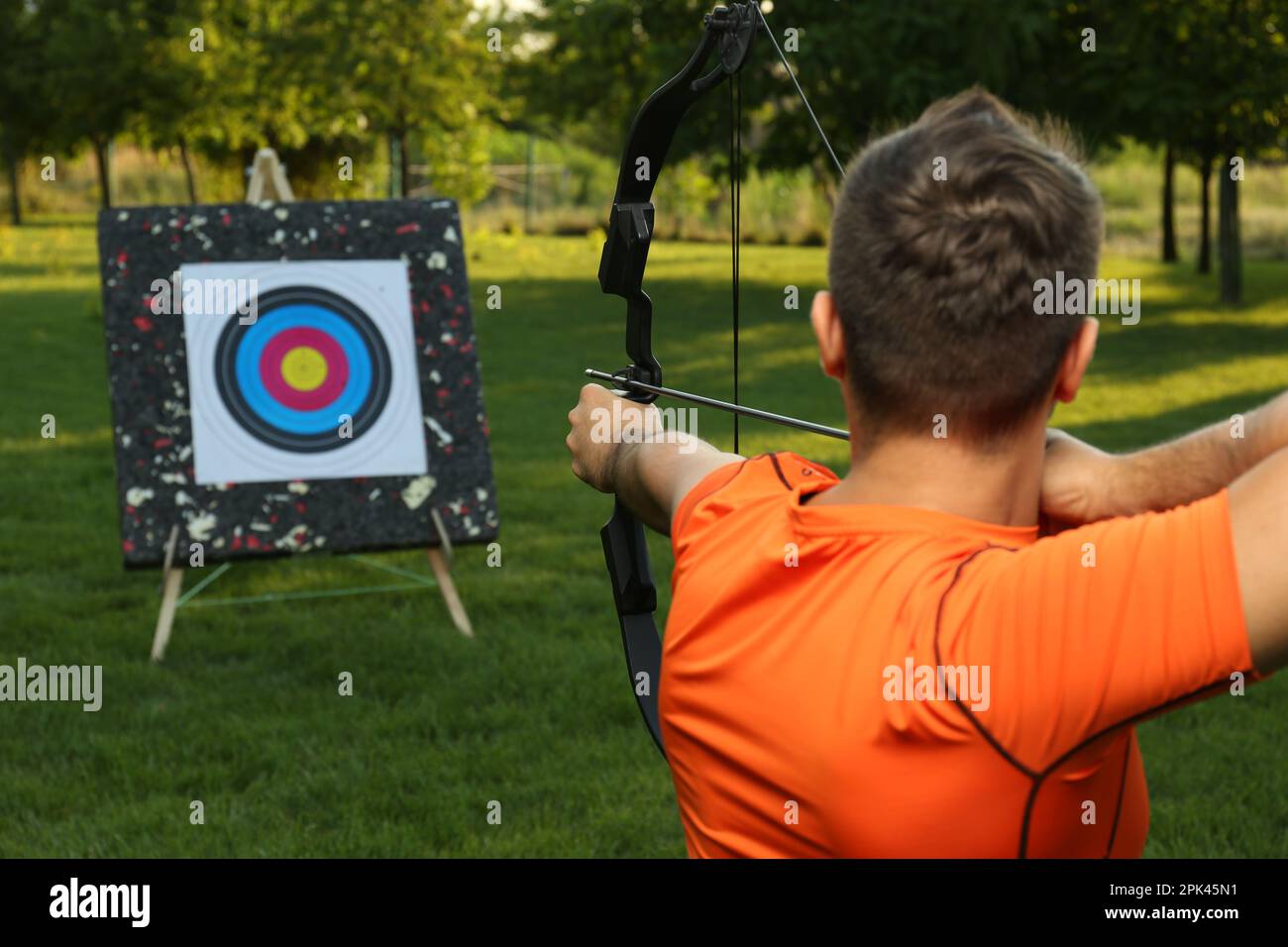 Man with bow and arrow aiming at archery target in park, back view ...