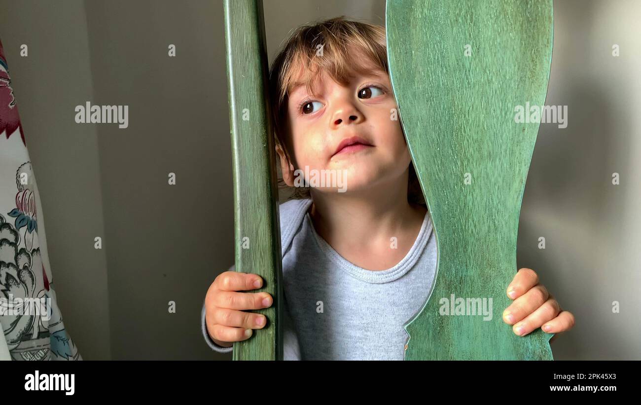 Baby child hides behind chair smiling at camera Stock Photo - Alamy