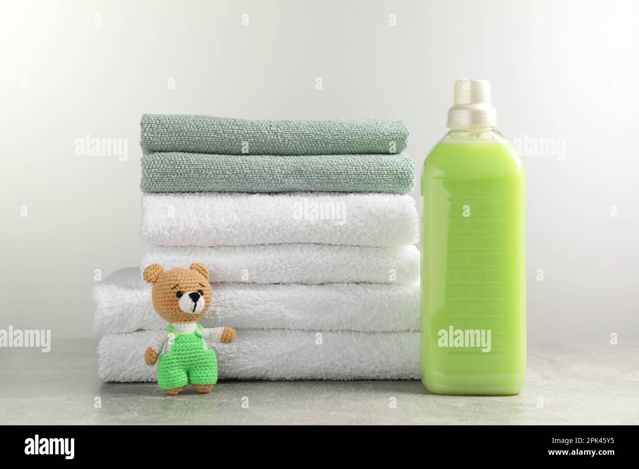 Bottle of laundry detergent, stacked fresh towels and knitted bear toy ...