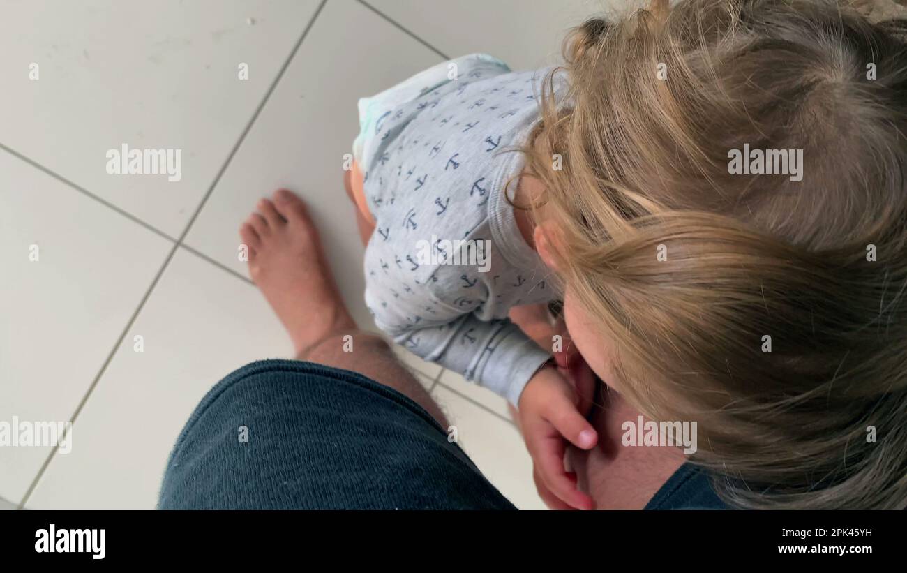 baby child holding into father legs looking up. Infant standing wanting ...