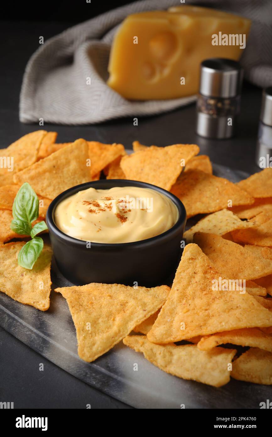 Delicious nachos and cheese sauce with basil on black table Stock Photo ...