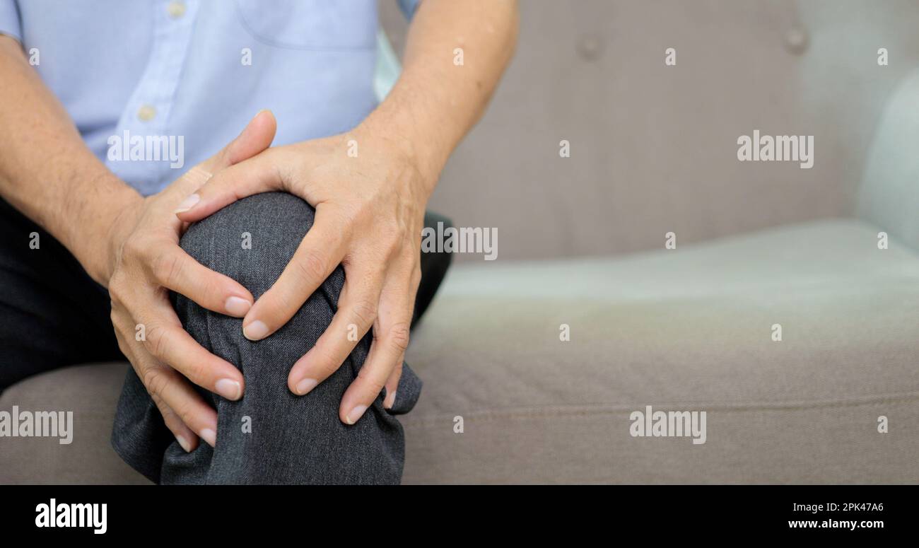 Close up shot of senior man suffering from knee pain sitting on sofa ...