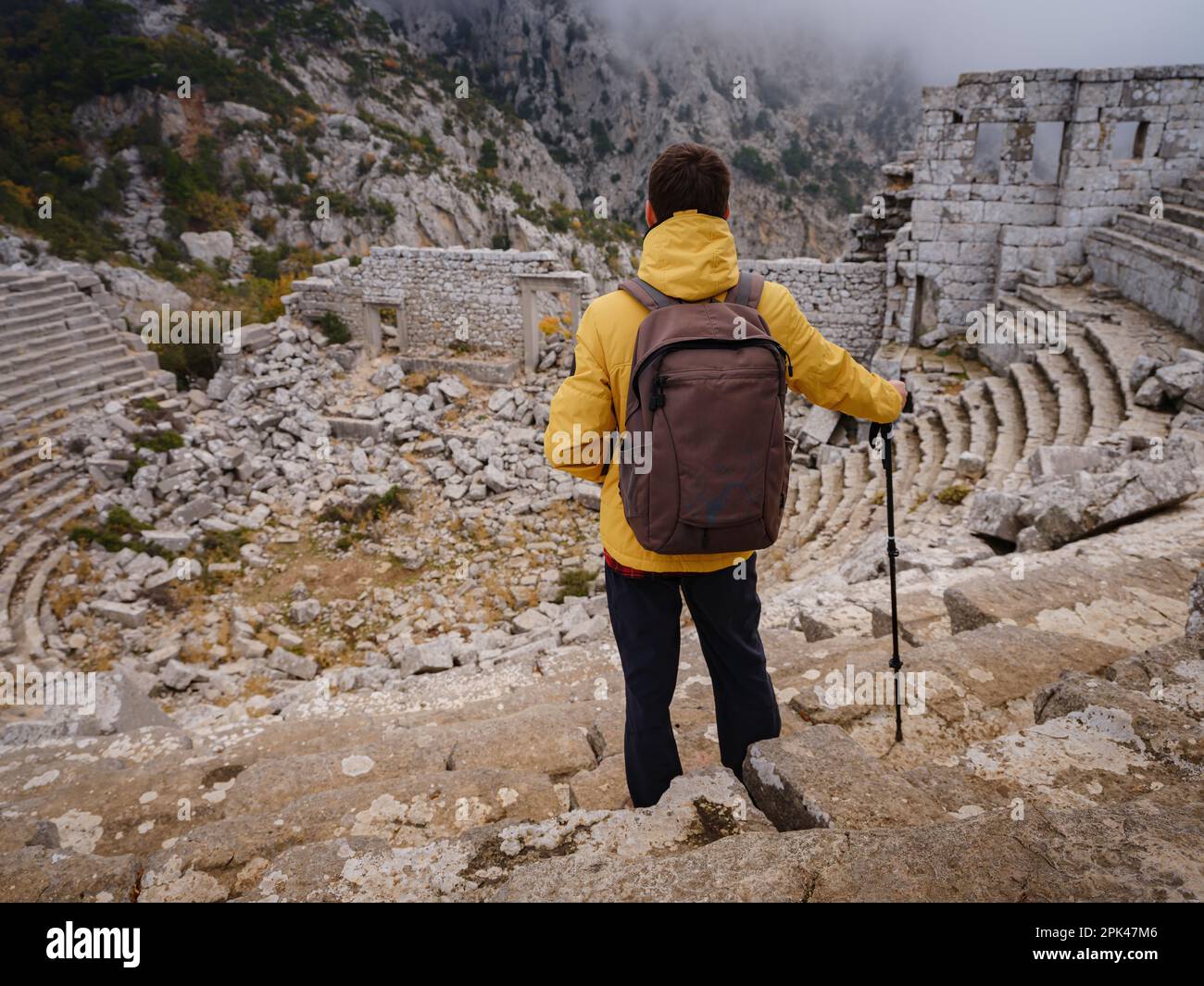 Autumn walk , man in yellow jacket looks at the ancient amphitheatre in ...