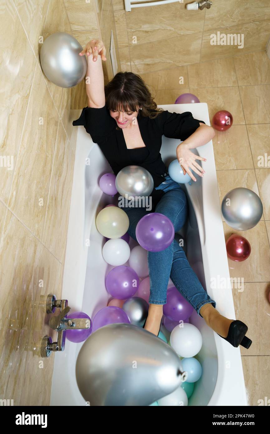 Young Woman Sitting in a Bathtub Full of Balloons in Bathroom Throwing ...