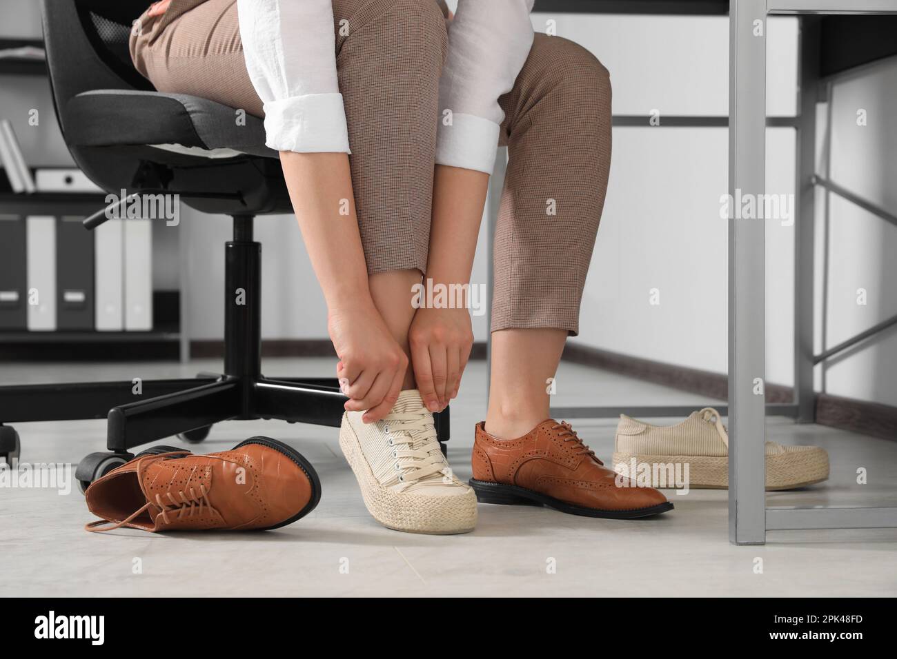 Woman taking off uncomfortable shoes and putting on sneakers in office ...