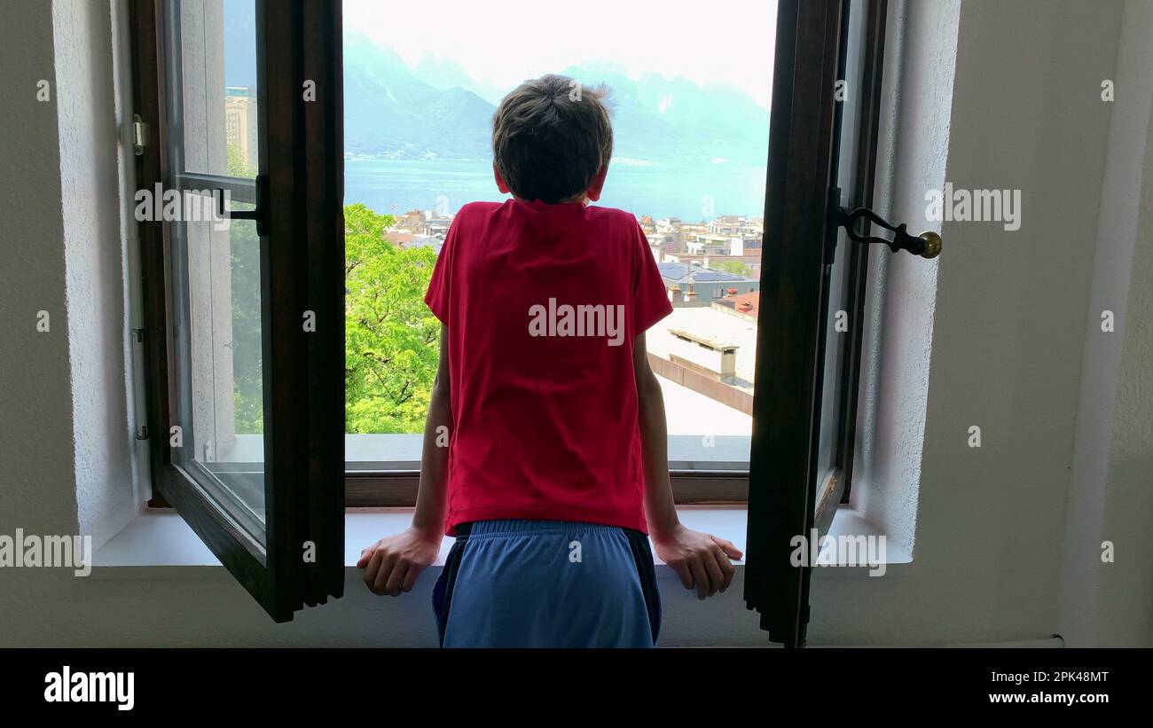 Child standing by window looking out. Boy looks outside, pensive kid ...