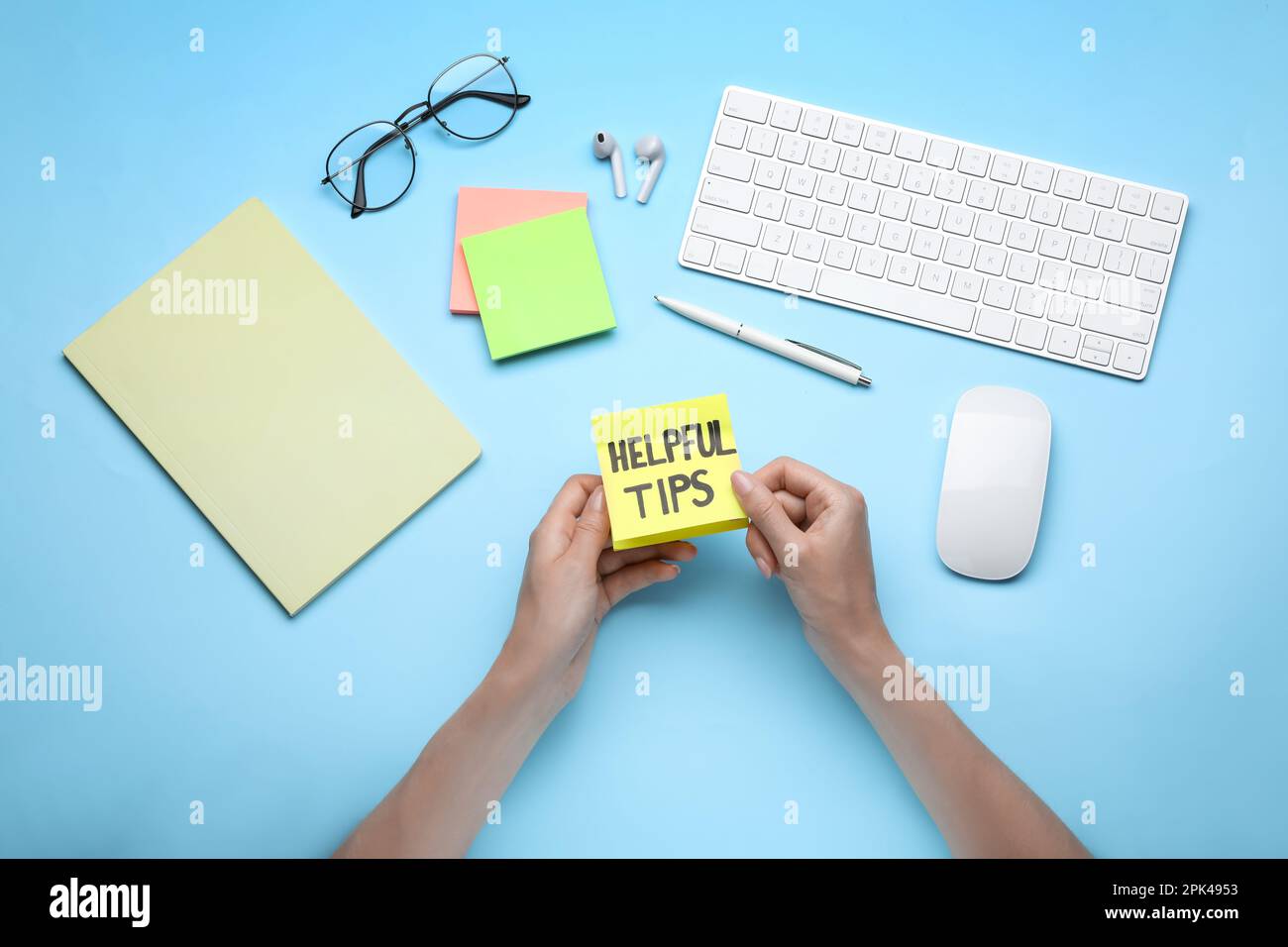 Woman holding paper note with phrase Helpful Tips at light blue table ...