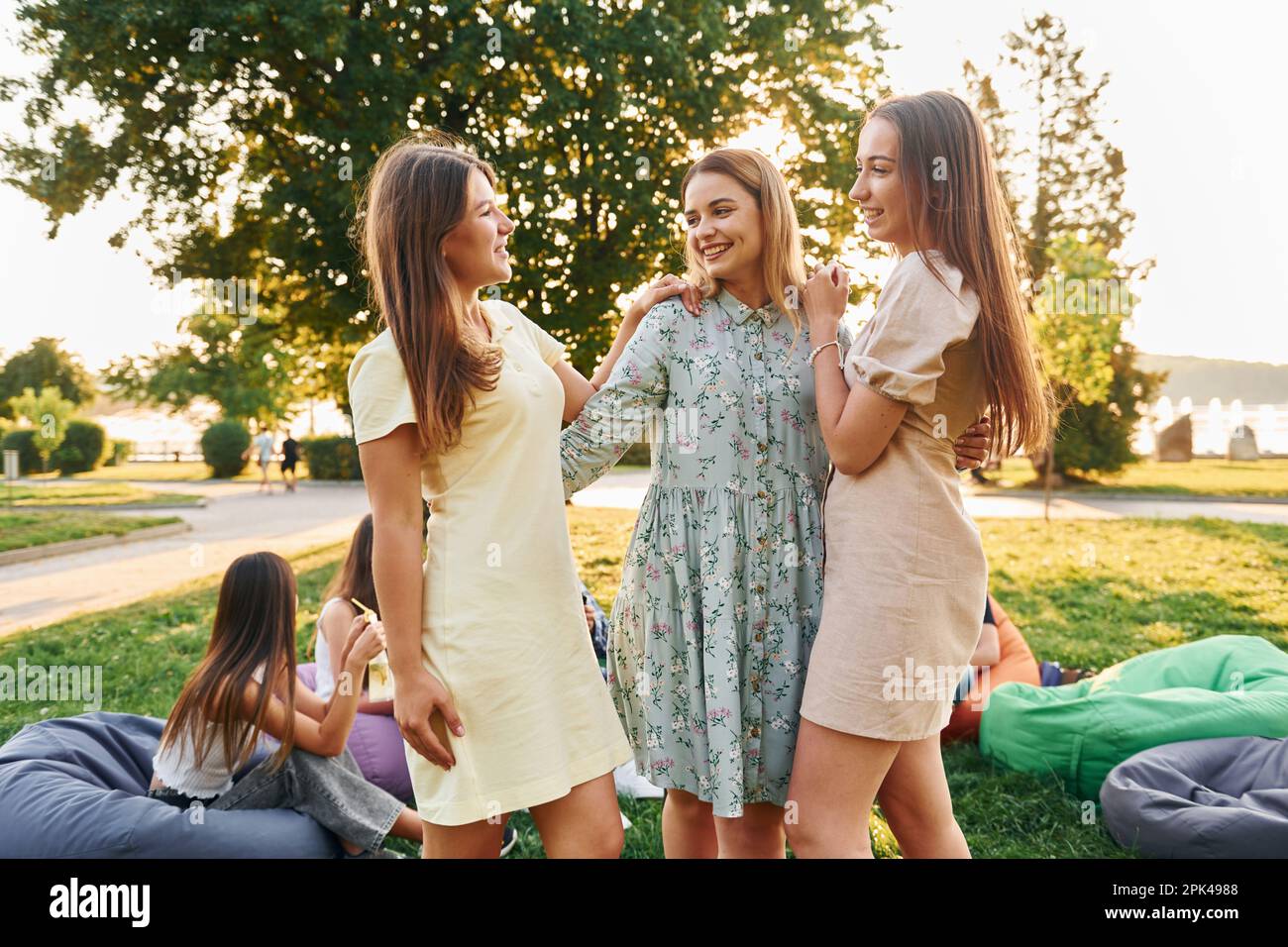 Female friends standing and having fun. Group of young people have a party in the park at summer ...