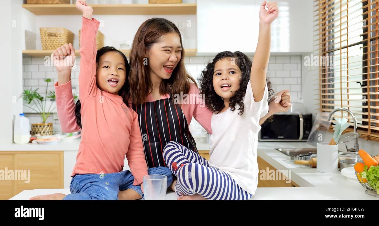 Duo girl rise hands up with mother cooking in kitchen, Family smiling ...