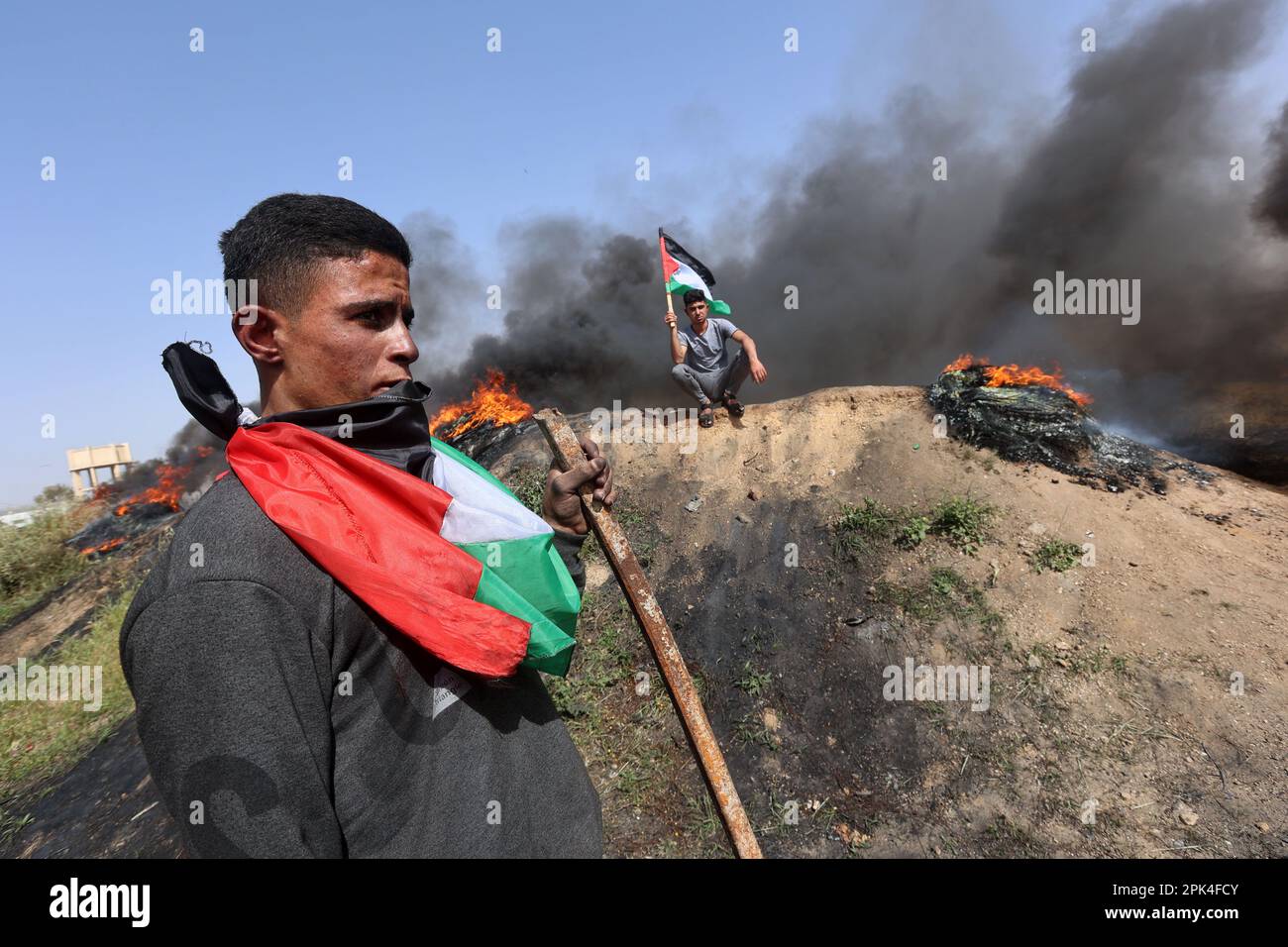 A Palestinian wearing a Palestinian flag as a scurf as they burn tires ...