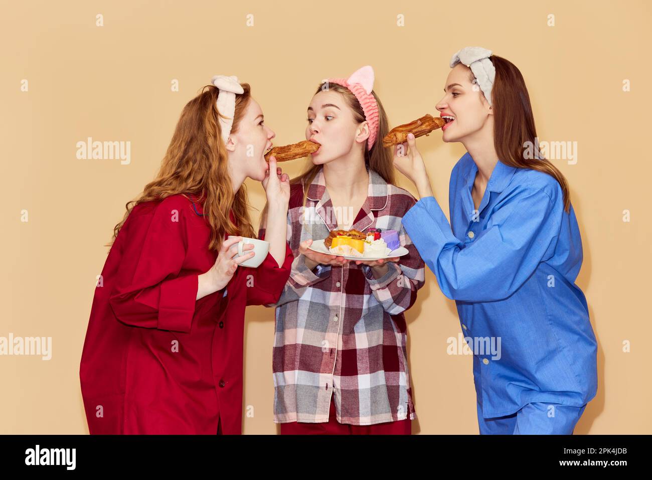 Sweet tooth. Beautiful young girls in comfortable pajamas eating sweets ...