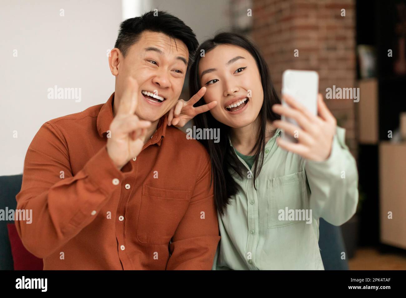 Excited asian couple taking selfie, gesturing peace signs, taking ...