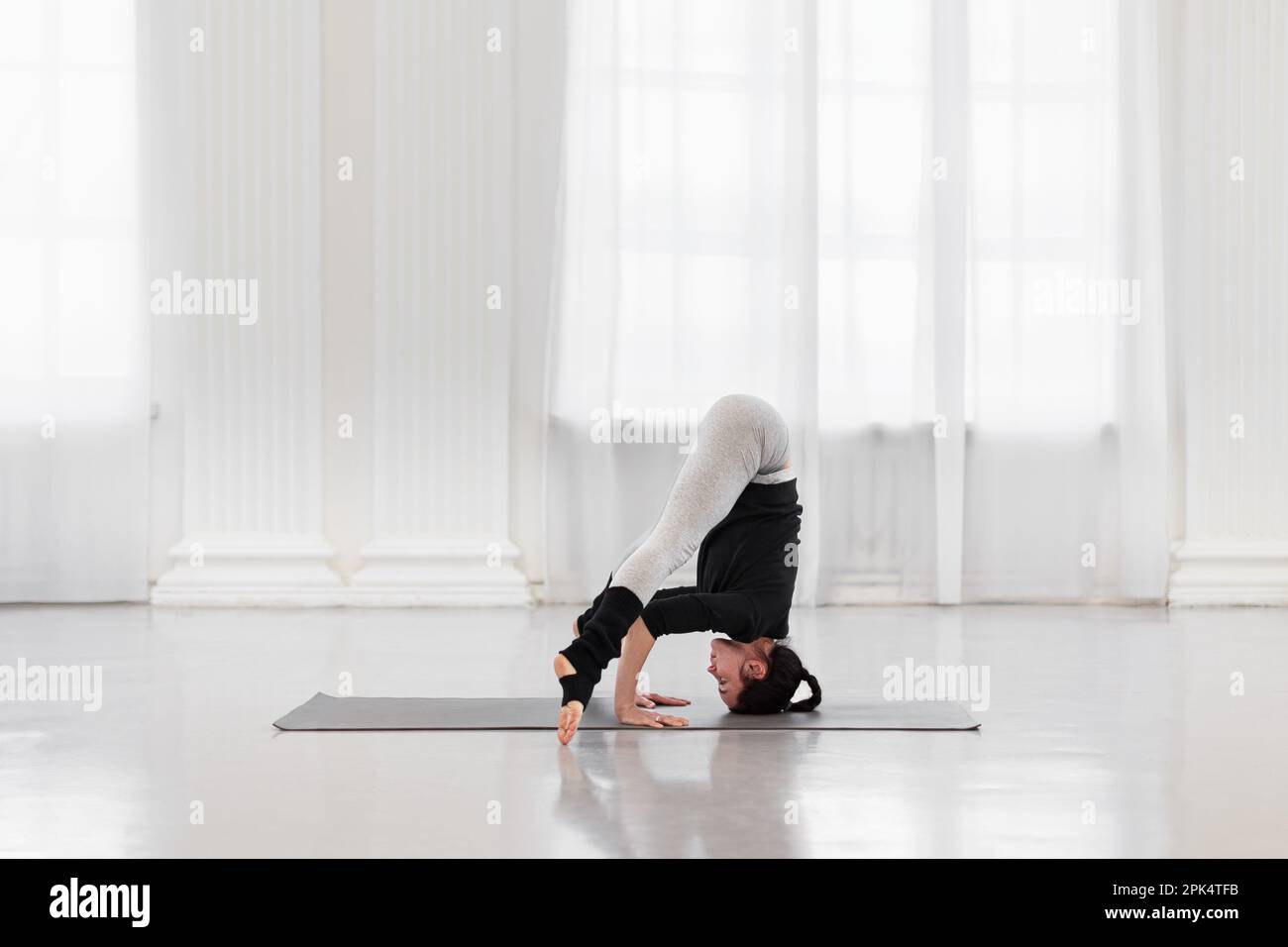 Slim young woman doing headstand preparation during yoga class in ...