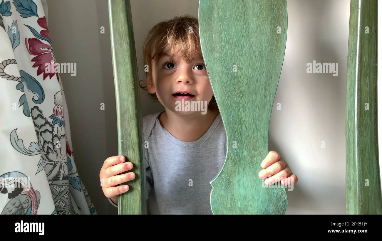 Cute adorable child infant boy hides behind chair furniture Stock Photo ...
