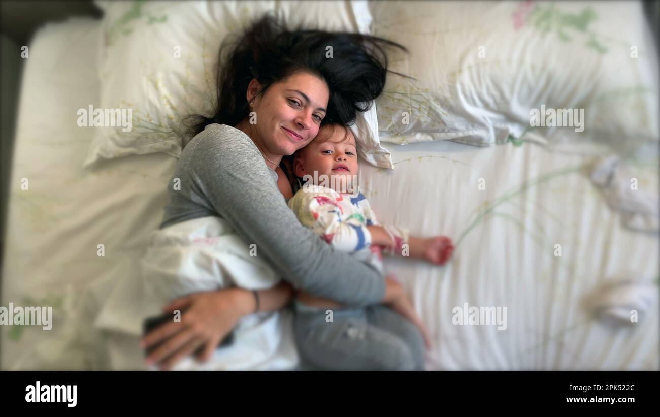 Mom and baby waving hello lying in bed together. Toddler boy and mother ...